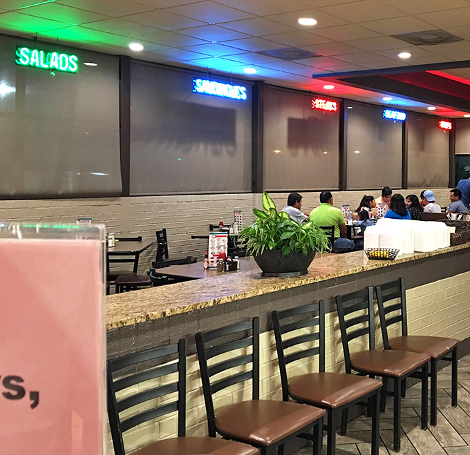 Colorful neon signs illuminate the dining area, creating zones of culinary possibility: SALADS, SANDWICHES, and other delicious territories to explore.