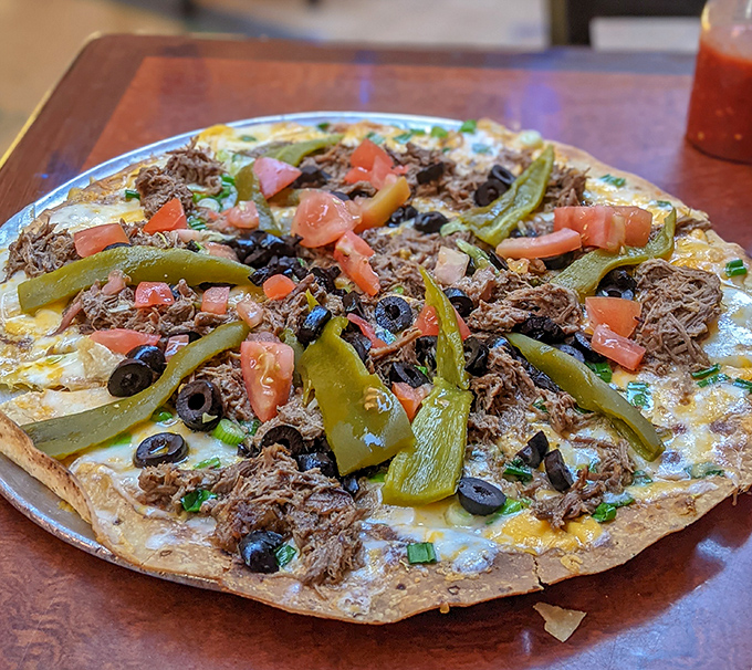 Not your delivery app's Mexican pizza—this handcrafted beauty showcases shredded beef, green chiles, and olives on a crispy canvas.