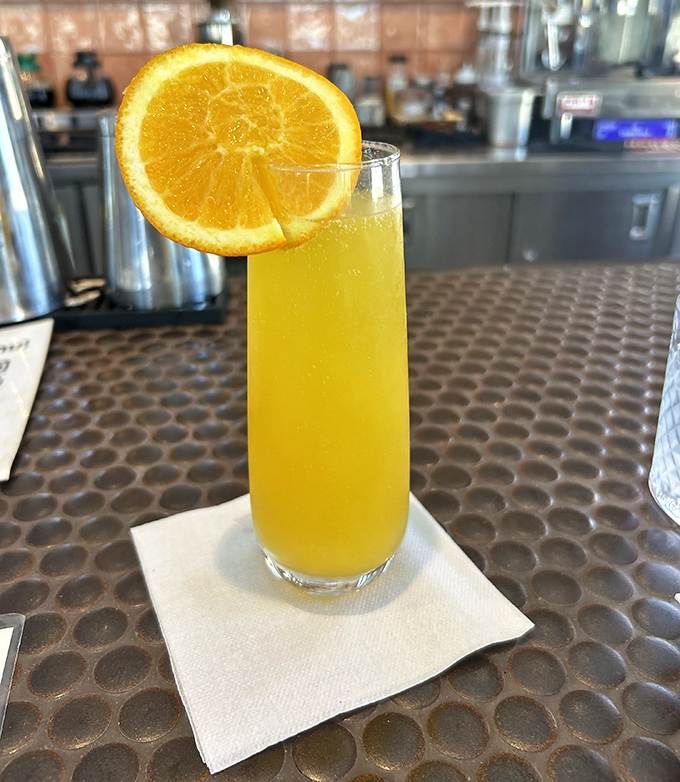 Sunshine in a glass! This mimosa stands tall and proud, wearing its orange slice like a jaunty hat on a Sunday morning.