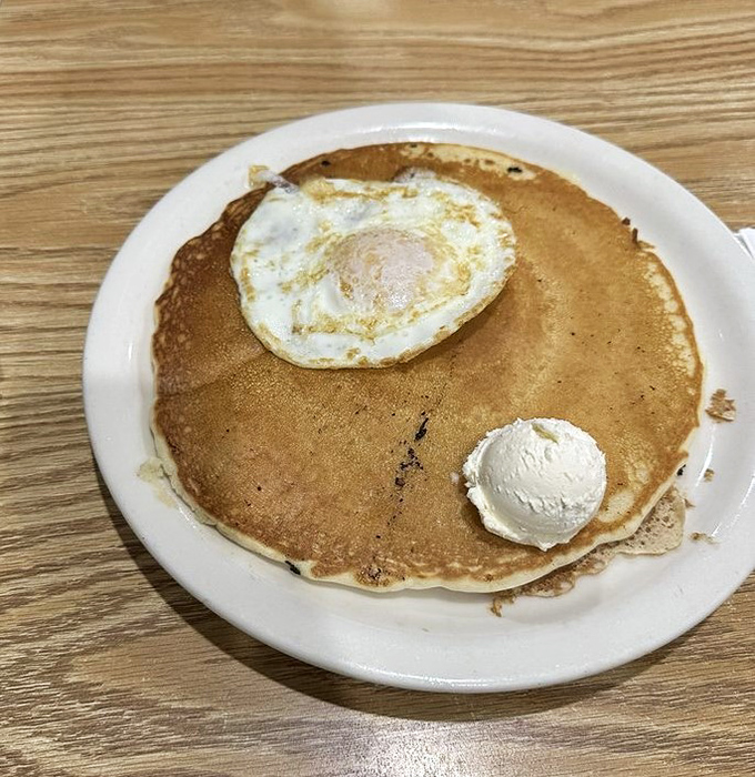 A pancake so perfect it deserves its own zip code, topped with an egg that's having a sunny-side-up day.