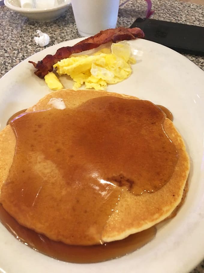 The humble pancake, transformed into a maple-soaked canvas of breakfast perfection, with eggs and bacon playing supporting roles.