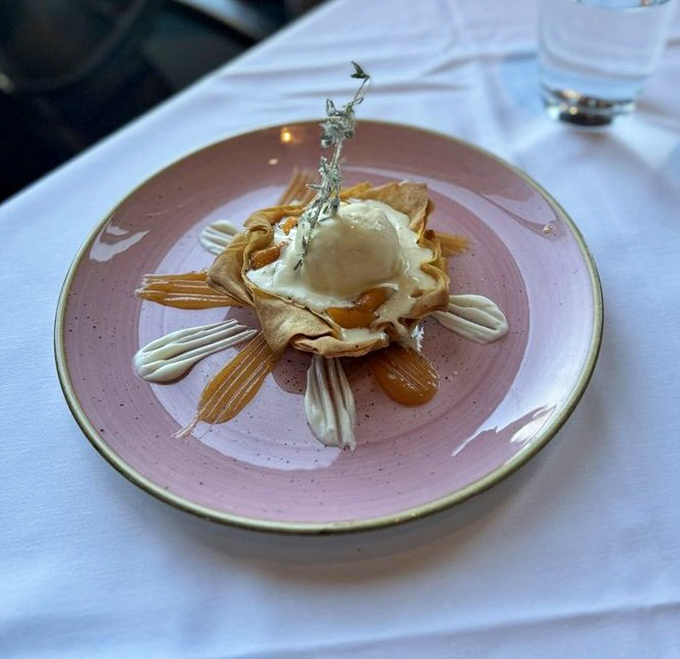 Dessert architecture that belongs in a museum &ndash; crispy phyllo cradling what appears to be ice cream, surrounded by artistic sauce flourishes.