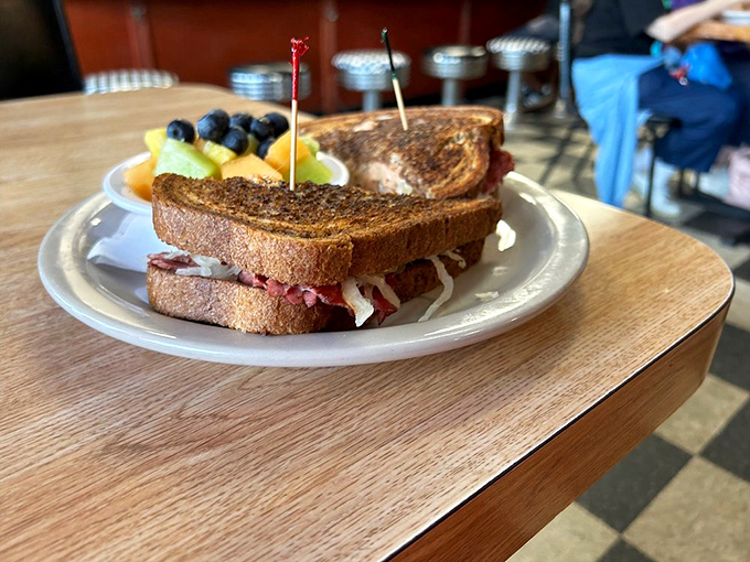 A Reuben sandwich with personality, accompanied by fresh fruit that makes you feel slightly virtuous about your lunch decisions.