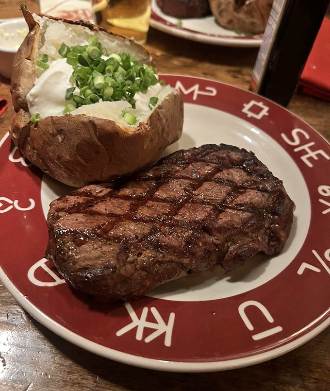 A ribeye with perfect grill marks that tell a story of fire-kissed flavor and a potato dressed better than most wedding guests.