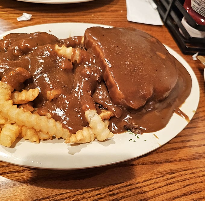 Hot roast beef sandwich with gravy cascading over the sides like a delicious waterfall. Those crinkle fries are about to take a delicious bath.