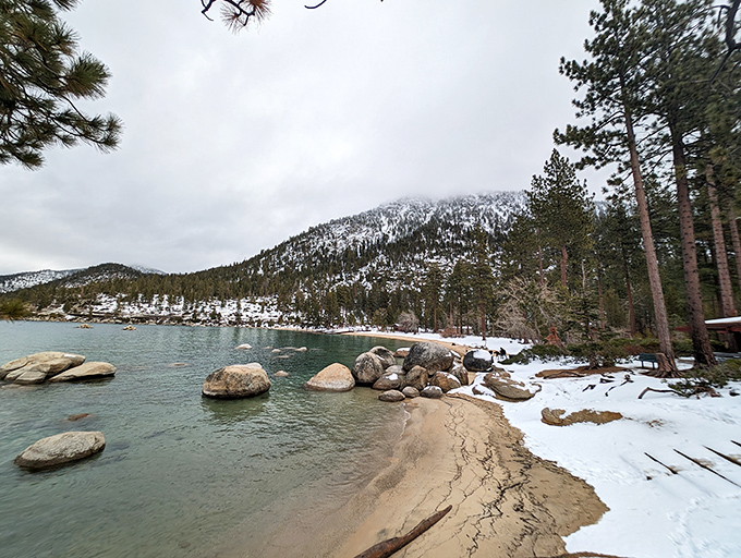 Winter transforms the shoreline into a postcard-worthy scene where snow meets sapphire water in stunning contrast and harmony.
