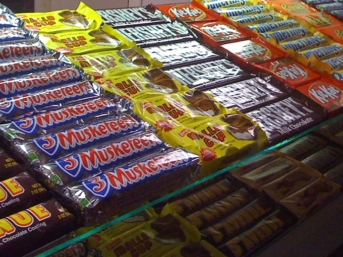 Candy bars lined up like sweet soldiers ready for deployment to eager moviegoers. The impossible choice between chocolate peanut butter and caramel crunch awaits.