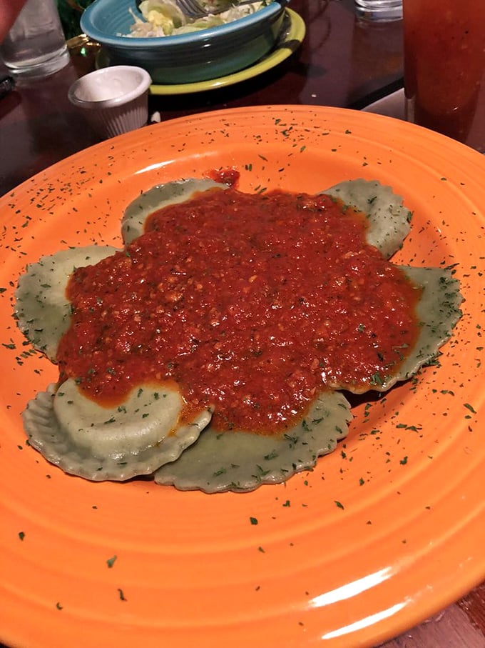 Green plate, green ravioli &ndash; a pasta pocket paradise filled with what appears to be spinach and ricotta, swimming in savory sauce.