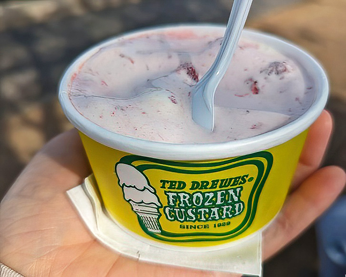 That iconic yellow cup holding strawberry-swirled dreams. The pink ribbons of fruit cutting through vanilla custard create a summer sunset you can taste.