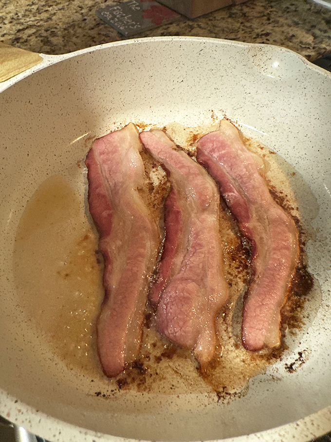 Sizzling bacon strips in their natural habitat – the cast iron skillet – moments before they transform into crispy, smoky perfection.