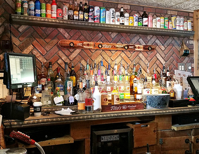 Bottles lined up like soldiers ready for duty. The herringbone brick backdrop adds rustic charm to this impressive liquid arsenal.
