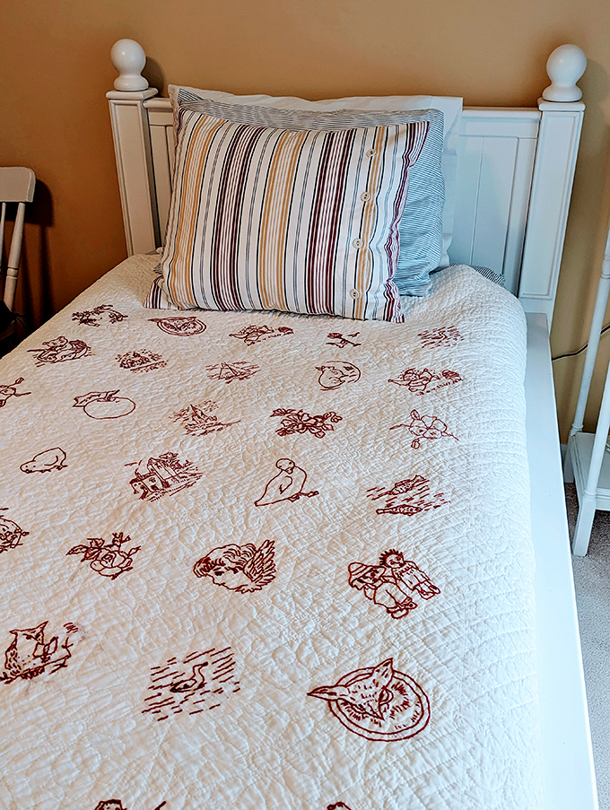 Handcrafted charm meets vintage comfort in this white bed frame showcasing a quilt with delightful redwork embroidery.