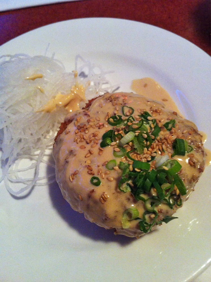 This crab cake isn't hiding behind filler &ndash; it's proudly showcasing its crabby personality with a crown of green onions.