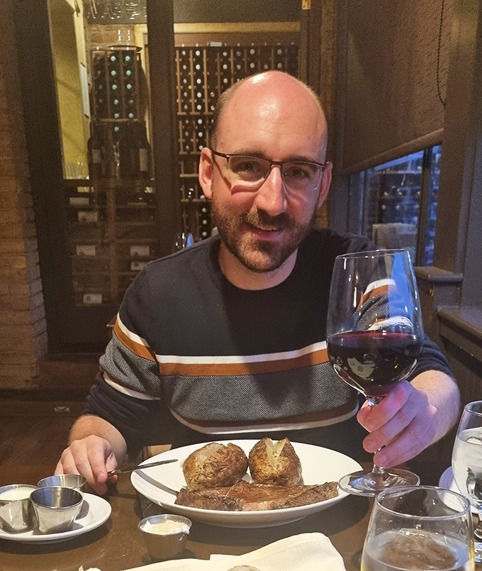 A dining companion enjoys the perfect pairing &ndash; a robust red wine alongside a steak that's clearly worth savoring slowly.