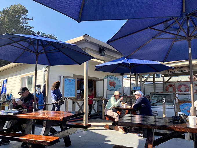 Blue umbrellas provide shade for the serious business of seafood enjoyment. The outdoor dining setup where strangers become friends over shared chowder enthusiasm.