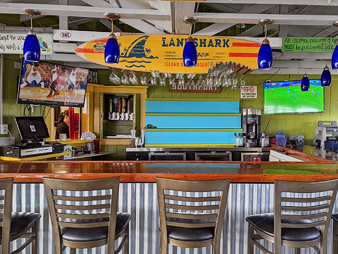 The bar's surfboard sign proclaims "Land Shark," while blue pendant lights hang like exotic jellyfish above seats that have hosted countless coastal stories.