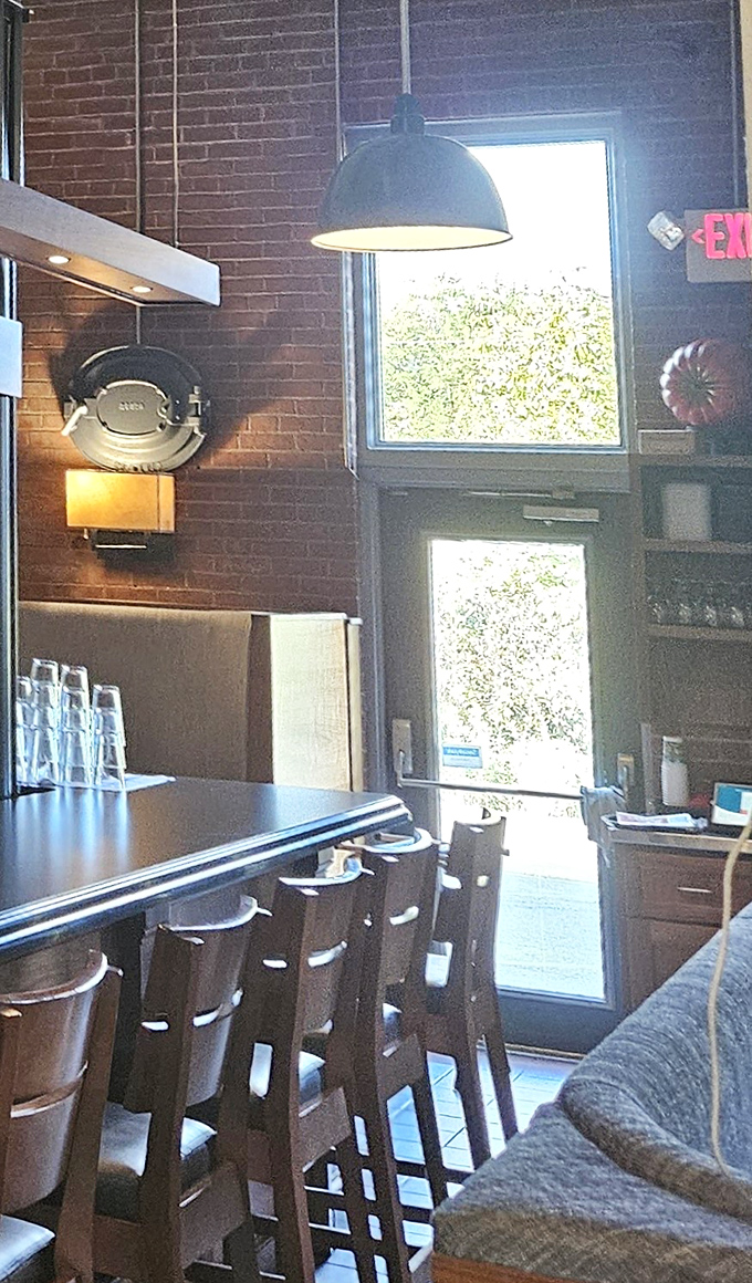 Tall windows flood the bar area with natural light, while exposed brick and vintage industrial elements create an atmosphere both authentic and inviting.