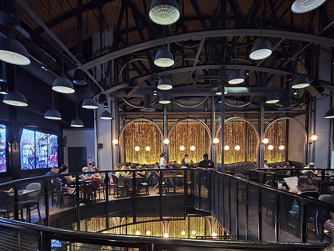 The soaring ceiling and golden backlit panels create a dining room worthy of a steampunk aristocrat. Multi-level seating ensures everyone gets a view of the spectacle.