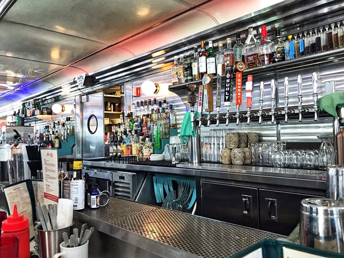 Behind the bar, bottles stand at attention like soldiers ready to serve. The chrome backdrop turns everyday bartending into theater.