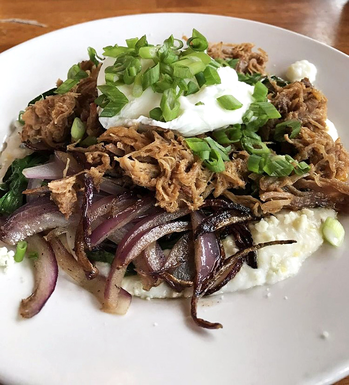 Slow-cooked meat atop creamy grits with caramelized onions &ndash; Southern comfort reimagined with the finesse of a culinary artist.