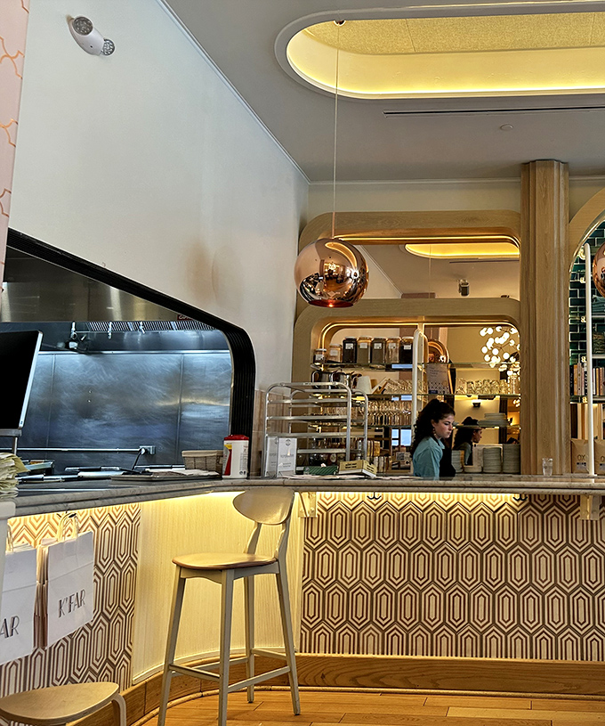 The counter area gleams with geometric patterns and warm lighting, showcasing pastries that practically beg you to point and say, "I'll take that one."