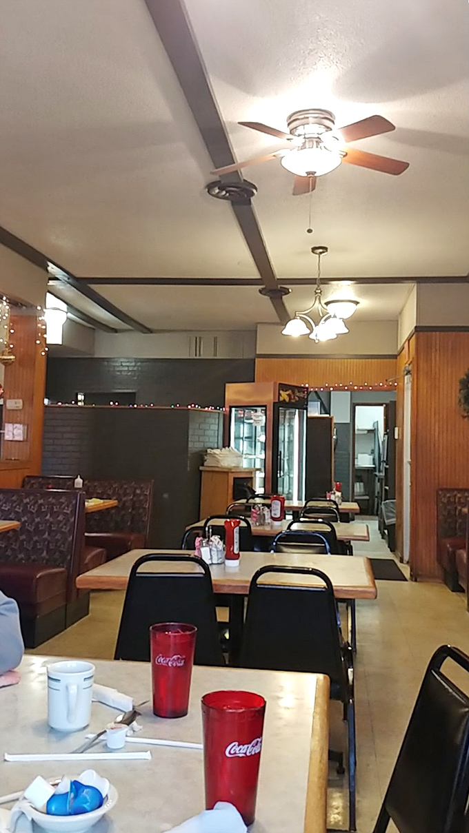 Red Coca-Cola glasses pop against wooden tables in a dining room where ceiling fans keep the air moving and conversation flowing. Classic Americana at its finest.