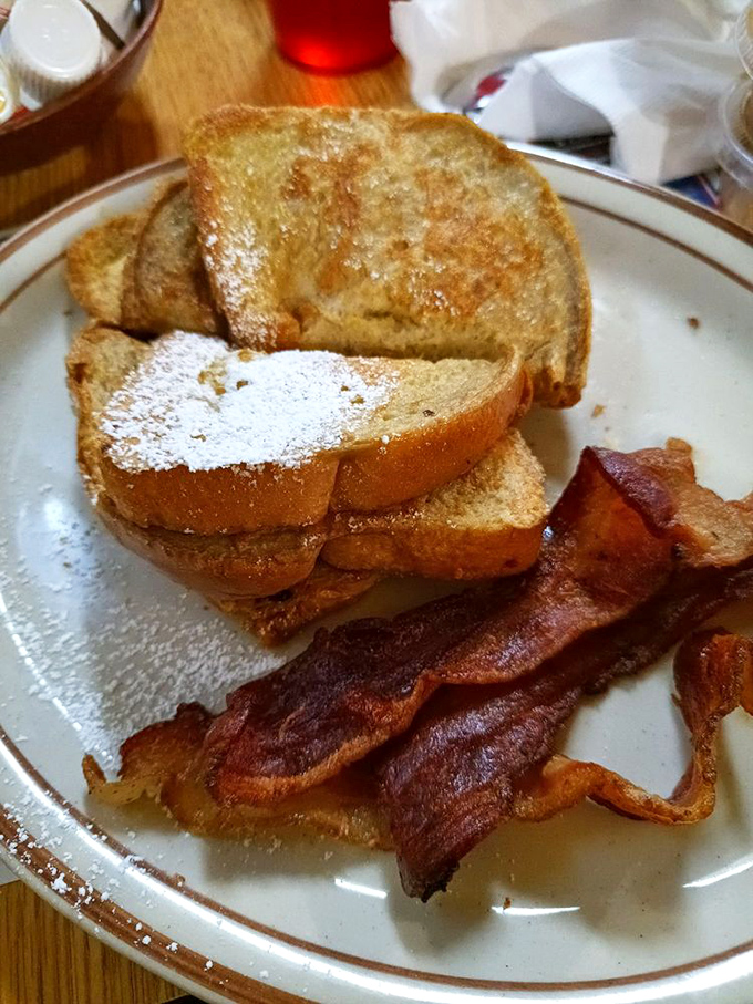 French toast dusted with powdered sugar like the first snow of winter, with bacon strips that have achieved that perfect crisp-yet-chewy texture science still can't explain.