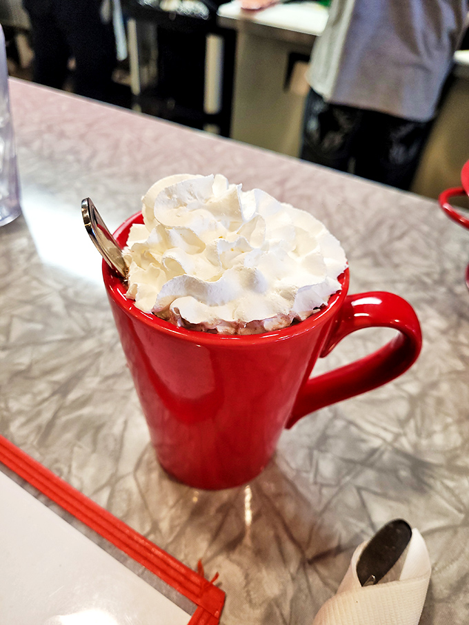 Hot chocolate topped with a cloud of whipped cream&mdash;winter comfort in a cheerful red mug that warms hands and hearts alike.