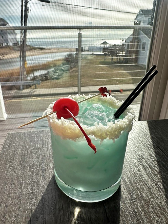 This blue cocktail with its coconut rim and cherry garnish isn't just a drink—it's a vacation in a glass. The ocean view provides the perfect backdrop.