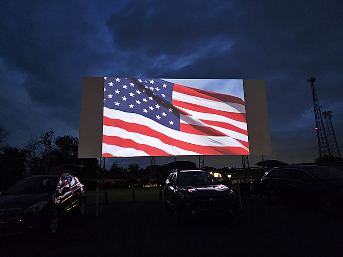 Old Glory illuminates the massive screen during the pre-show, a patriotic tradition that feels as American as the drive-in experience itself.
