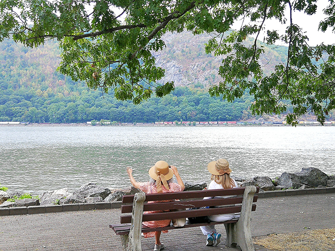 Two visitors enjoying the simple luxury of a riverside bench—proving sometimes the best vacation moments cost absolutely nothing.