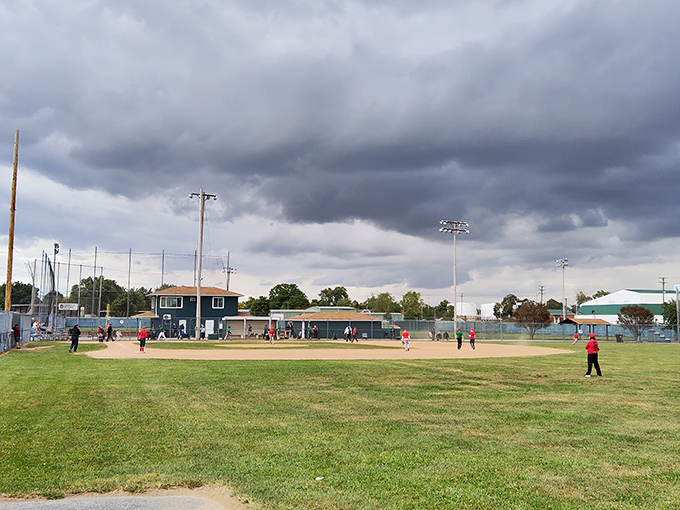Community baseball under dramatic skies&mdash;where kids learn teamwork and parents practice the art of supportive sideline coaching.