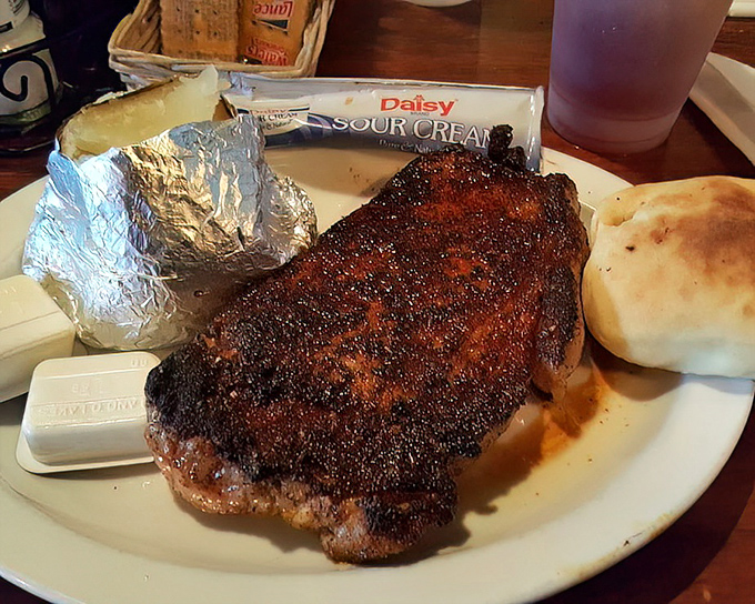 This ribeye doesn't just sit on the plate&mdash;it commands attention with its perfect seasoning and juicy promise. The foil-wrapped potato stands by like a faithful sidekick.