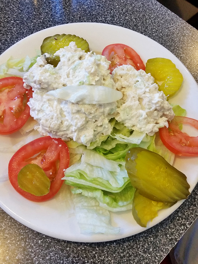 A chicken salad that proves diners understand balance&mdash;creamy protein nestled on crisp lettuce with fresh tomatoes and pickles providing that perfect acidic counterpoint.