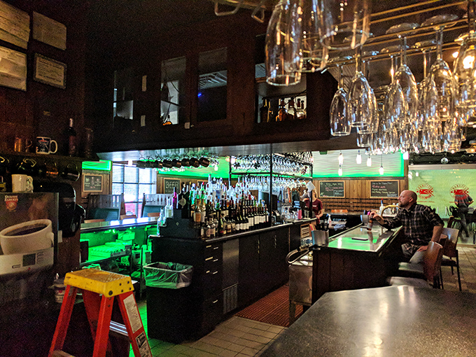 The bar glows with emerald light, wine glasses hanging overhead like crystal stalactites in this cave of liquid treasures.