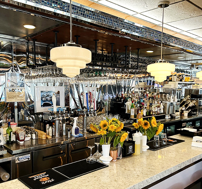 The bar area gleams with promise, sunflowers adding warmth to the polished chrome. Where cocktails meet milkshakes in the great democracy of diner drinking.