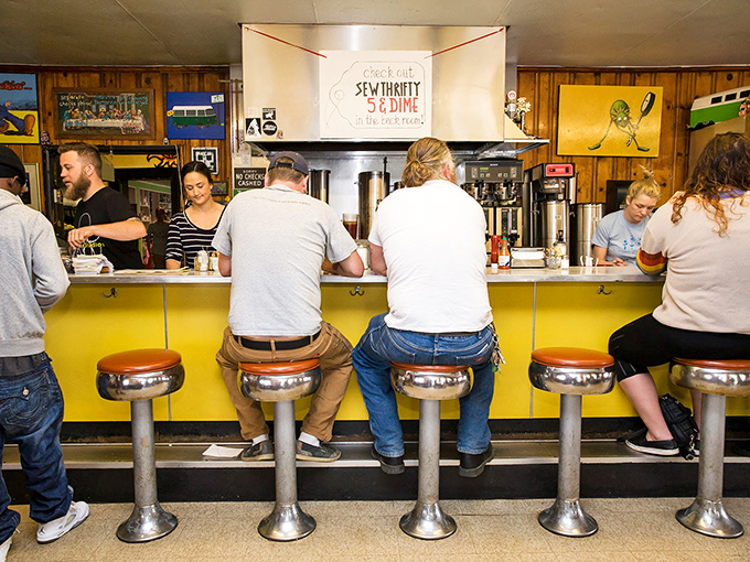 Classic diner counter service where regulars perch on chrome stools beneath the quirky "SEW THRIFTY STUMP" sign.