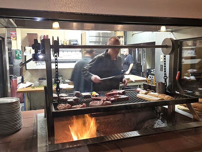Behind the glass, culinary magic happens over dancing flames. This isn't cooking; it's performance art with delicious consequences.