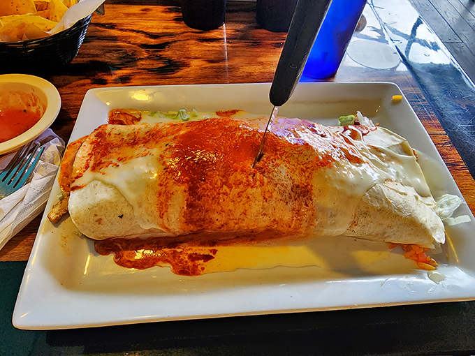 This burrito isn't just wrapped&mdash;it's swaddled, tucked in, and lovingly bathed in red sauce. The knife standing upright is both a serving suggestion and a warning of its substantial girth.