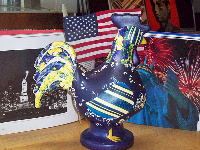A fabric-covered rooster with more personality than some people I know, standing proudly beside patriotic memorabilia.
