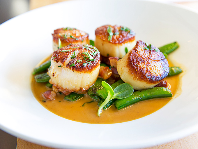 These seared scallops have achieved the impossible – golden-brown perfection while remaining tender within, swimming in a sauce worth bottling.