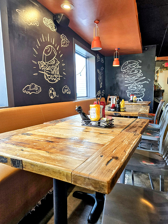 Rustic wooden tables against chalkboard walls with burger art&mdash;this isn't just decor, it's a visual appetizer before the main event arrives.