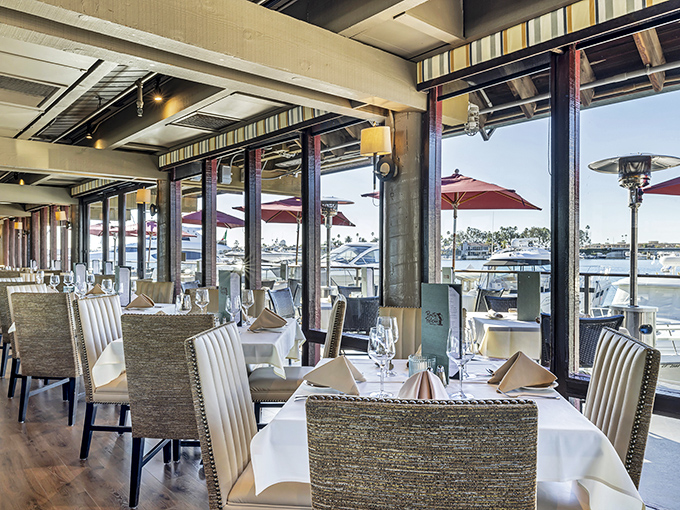Another angle reveals the thoughtful coastal design, where comfortable seating meets elegant touches and those ever-present waterfront windows beckon diners.