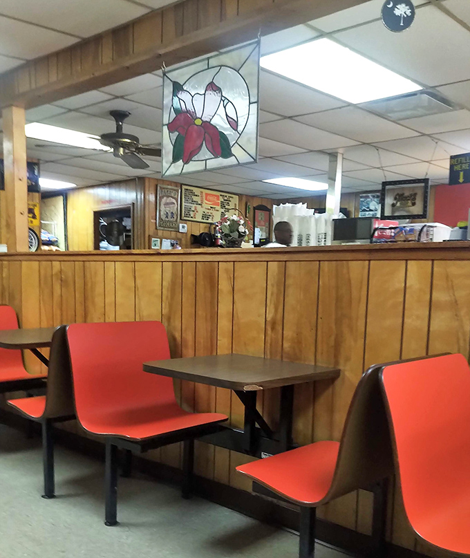 Those red chairs have supported generations of happy diners, while that poinsettia stained glass adds a touch of unexpected elegance to burger paradise.