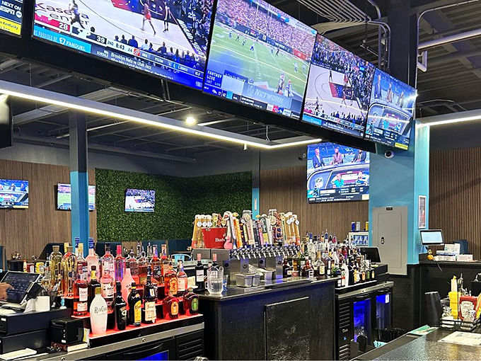 The well-stocked bar gleams beneath multiple screens, creating that perfect sports-viewing environment where no game goes unwatched and no thirst goes unquenched.
