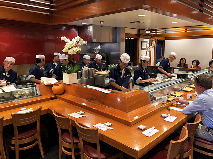 The sushi bar&mdash;where magic happens in plain sight as chefs transform simple ingredients into edible poetry under the warm glow of wooden accents.