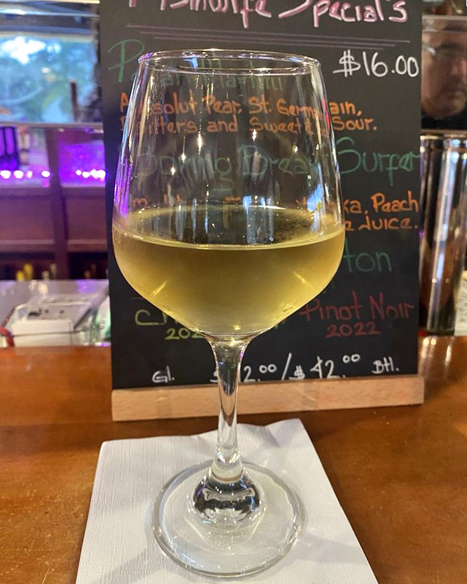 A glass of Bernardus Chardonnay catching the light, while the chalkboard behind hints at other liquid treasures awaiting discovery.