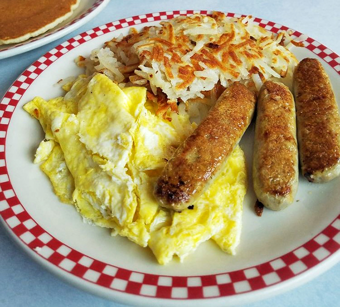 Breakfast trinity: eggs, sausage, and hash browns&mdash;the holy alliance that makes mornings bearable. Simple perfection on a red-rimmed plate.