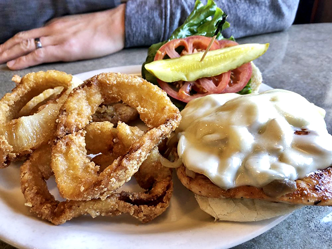 A sandwich with melty cheese cascading down its sides like a dairy waterfall, paired with onion rings that deserve their own fan club.