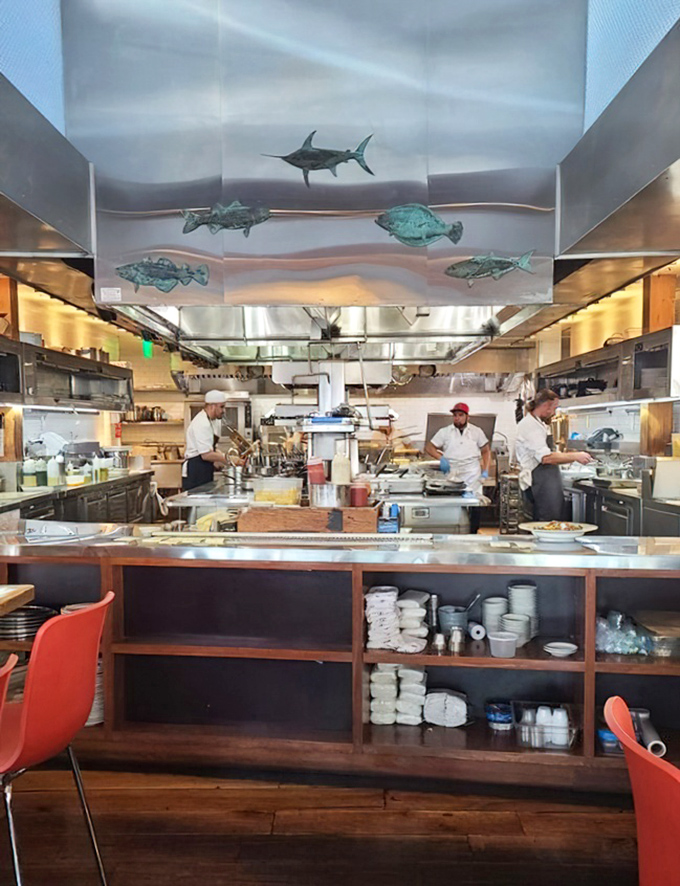 The open kitchen with its fish silhouettes overhead isn't just for show—it's theater where every sizzle and steam tells the story of your dinner.